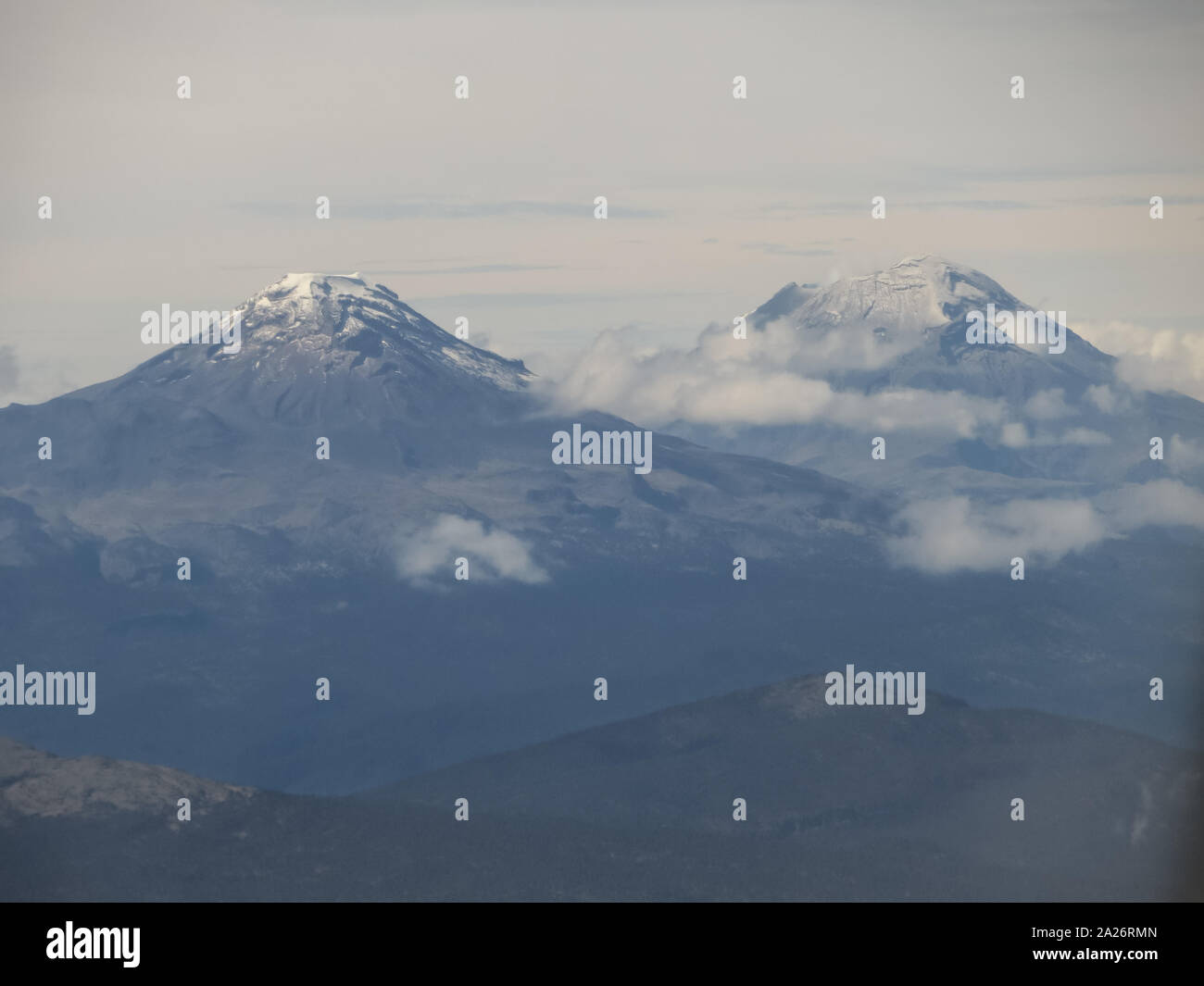 View of two majestic volcanoes with snowy peaks surrounded by clouds ...
