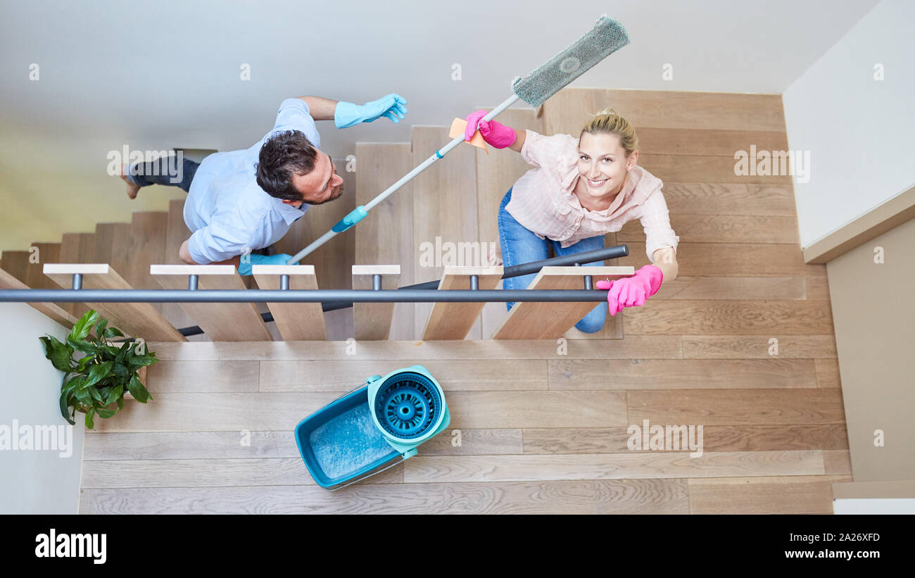 Young couple kidding around with mop while cleaning stairs in stairway ...