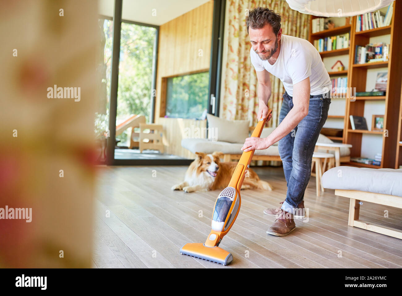 Houseman with vacuum cleaner vacuuming the floor in the living room ...