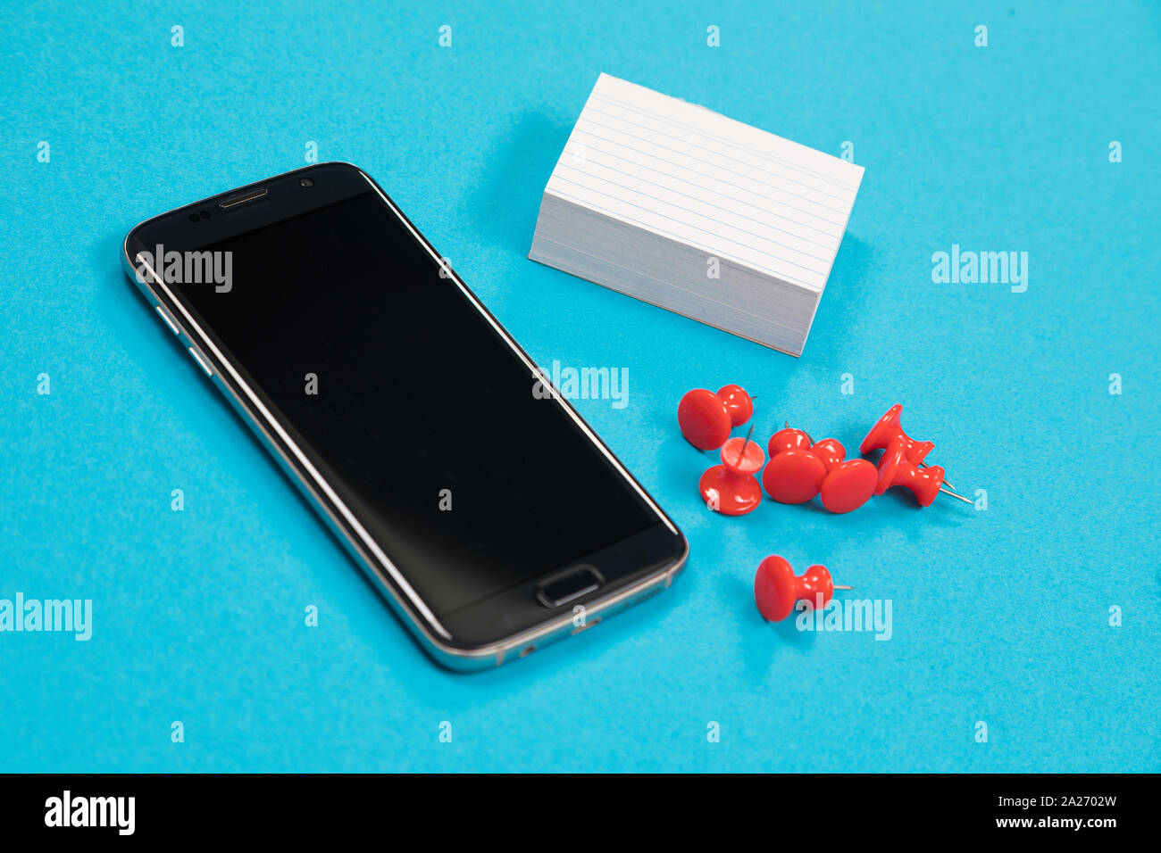 Black mobile phone, a pile of white scratch paper and red push pins are ...