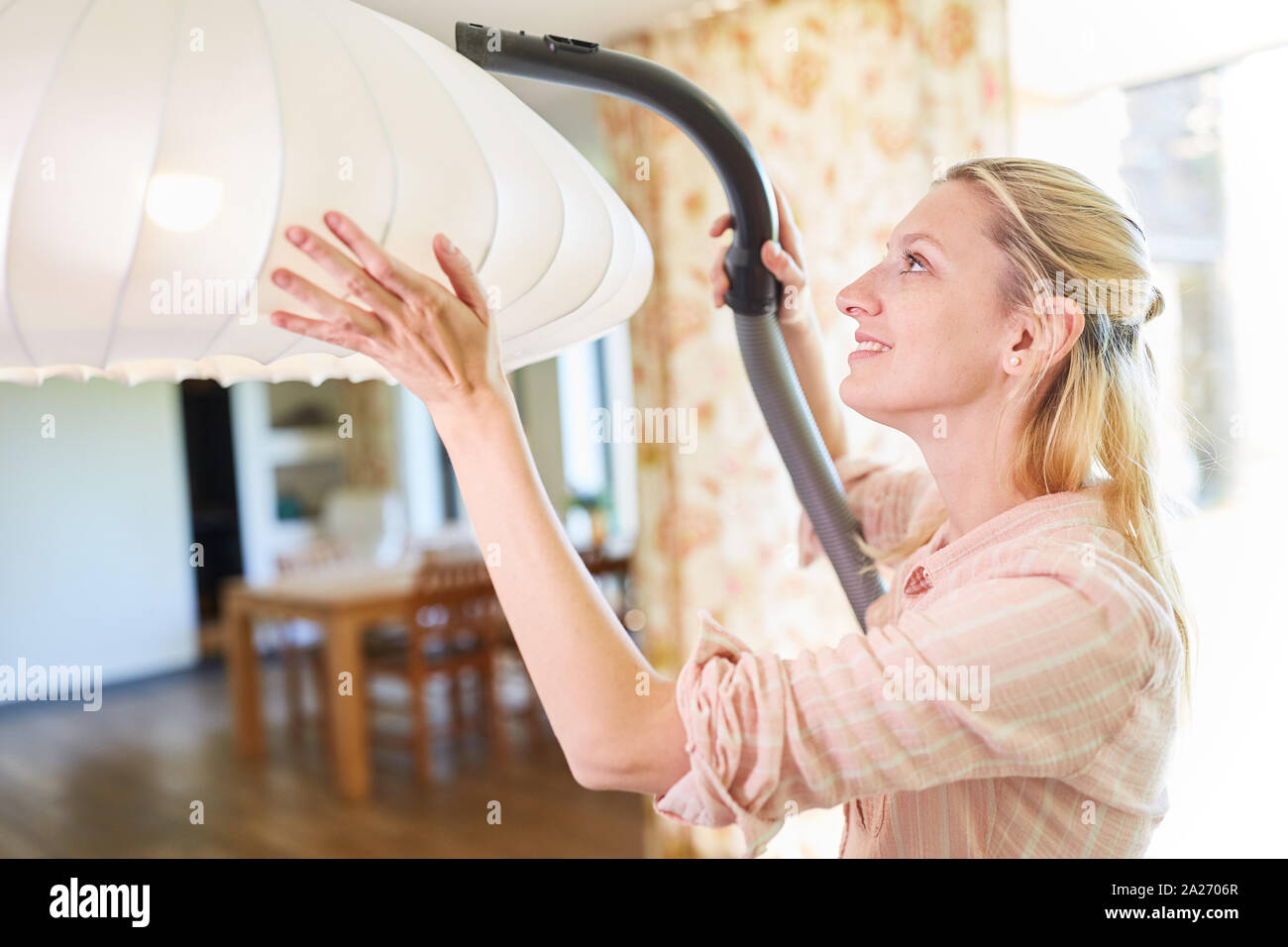 Woman as a cleaning lady or domestic help vacuuming a hanging lamp ...