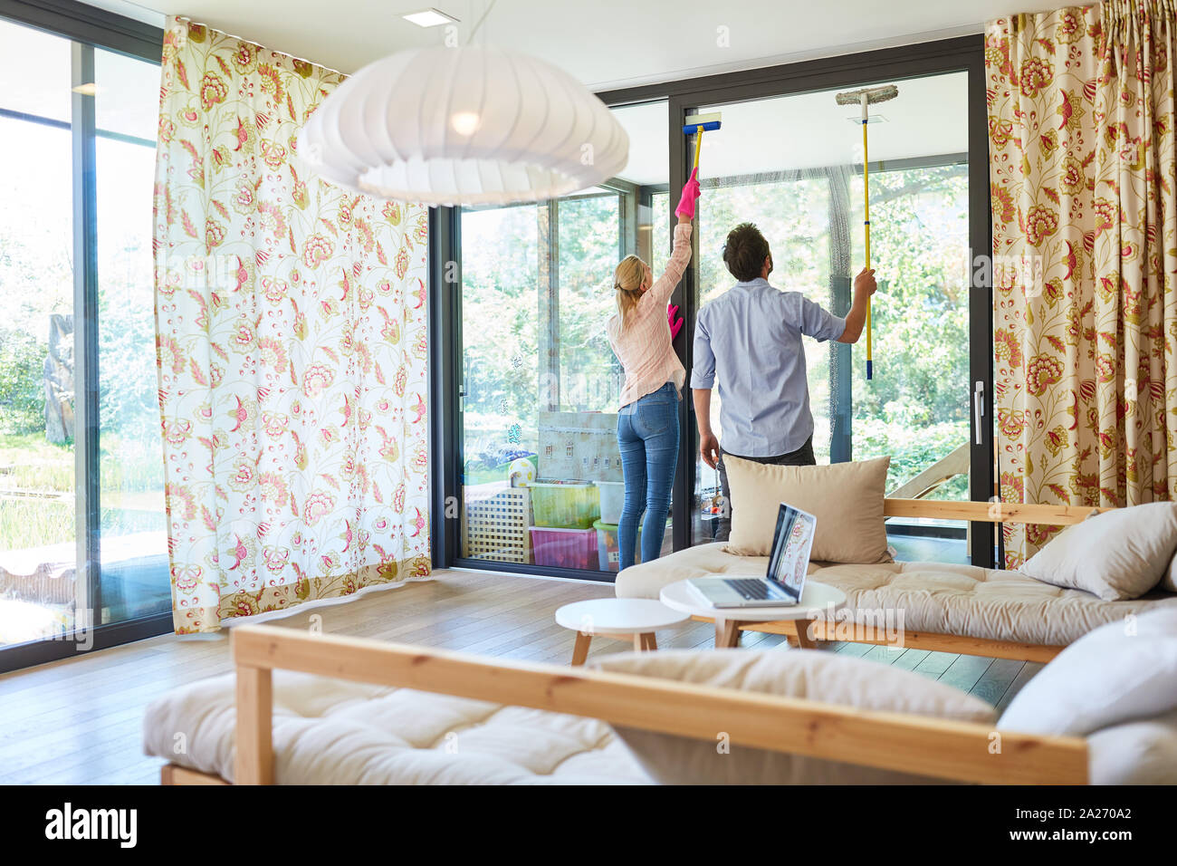 Young couple cleaning house together in the living room by the window ...