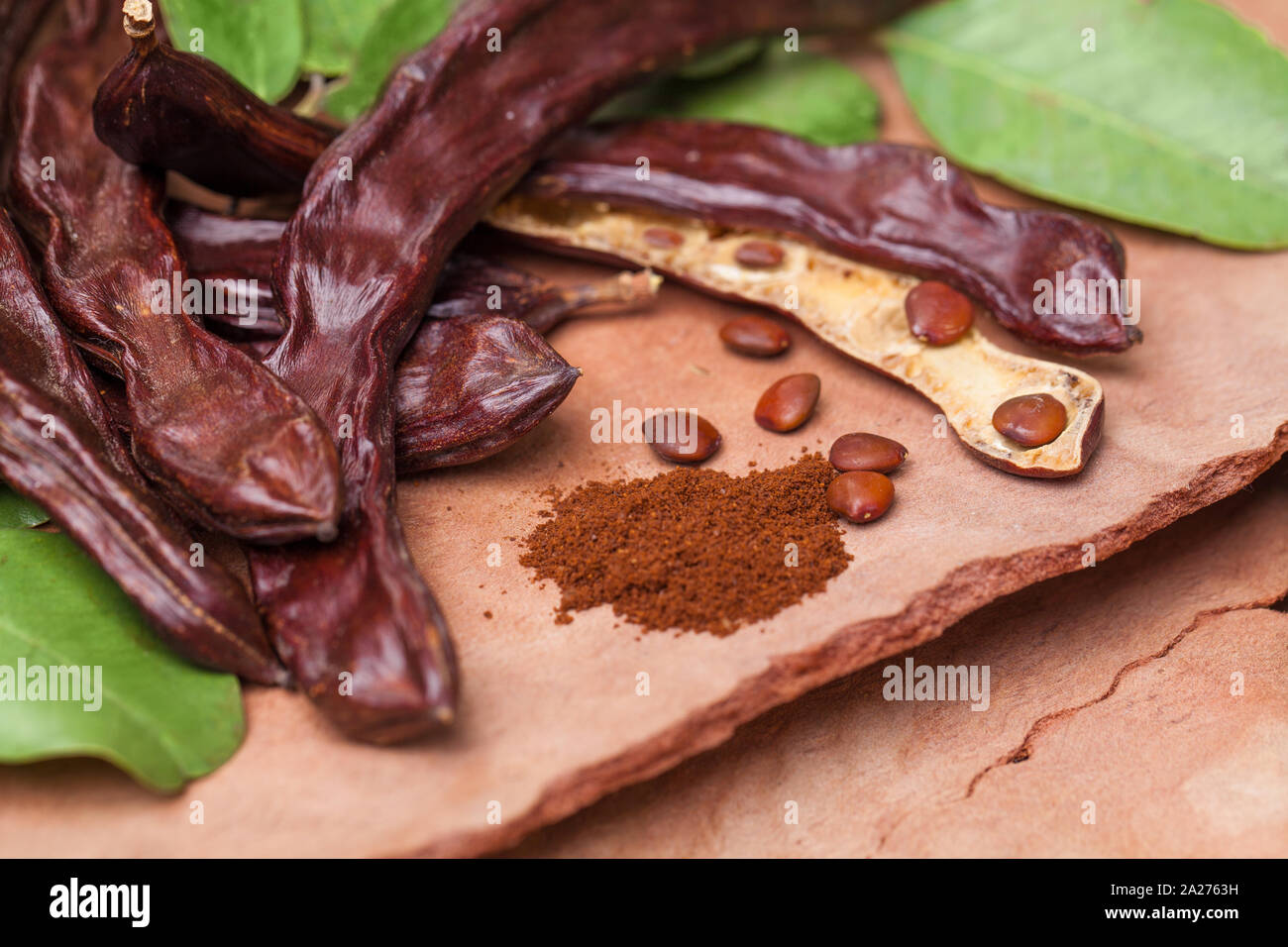 Carob. Organic carob pods with seeds and leaves on tree bark table ...
