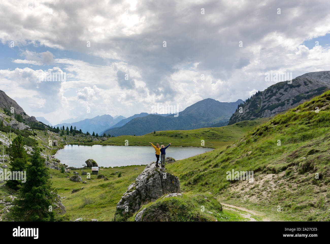 two female hikers stand on a boulder in a pretty mountain landscape in ...