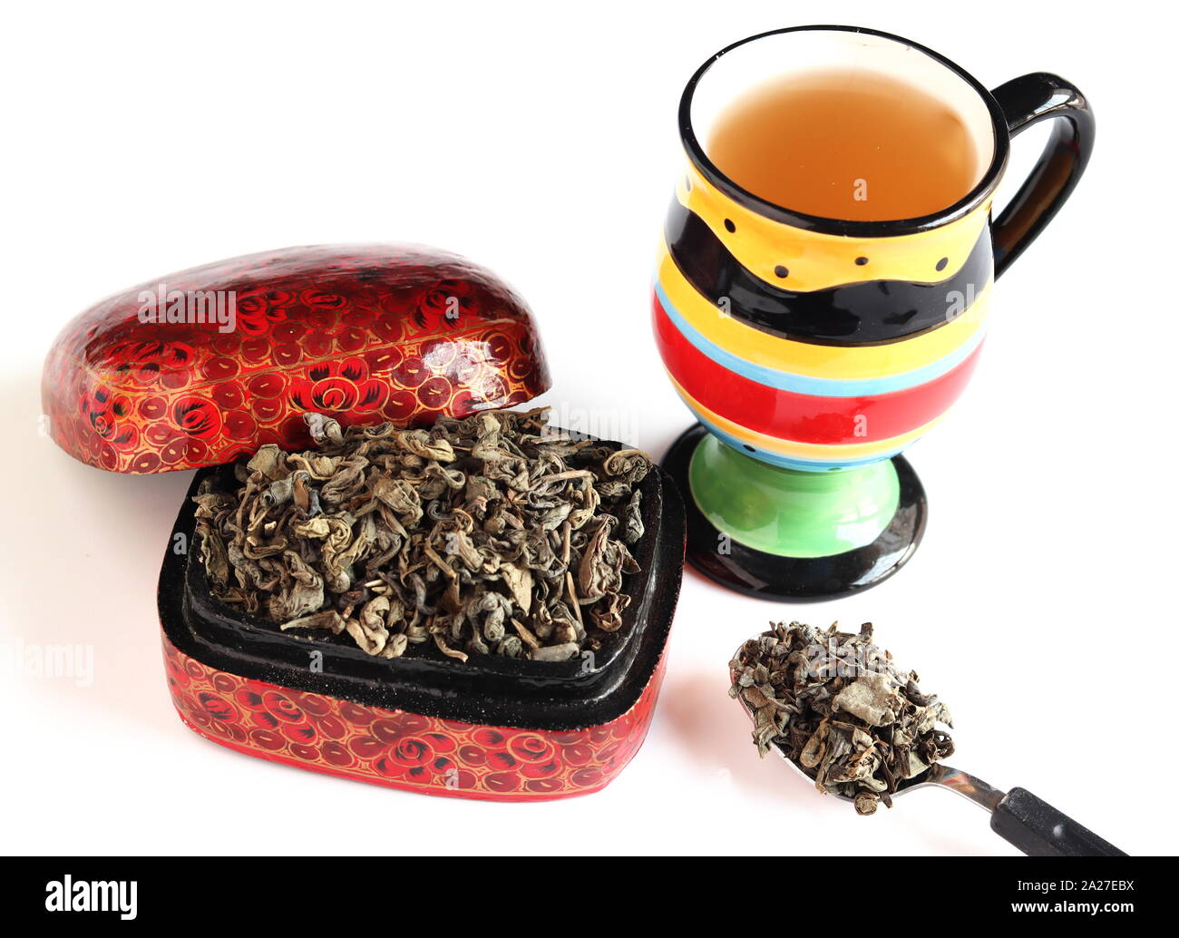 Loose green tea leaves in red box with colourful mug on white ...