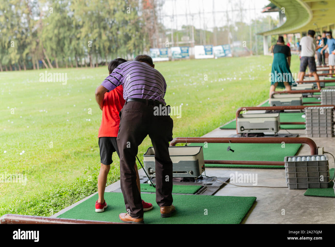 Personal trainer giving lesson to young boy in golf driving range Stock ...