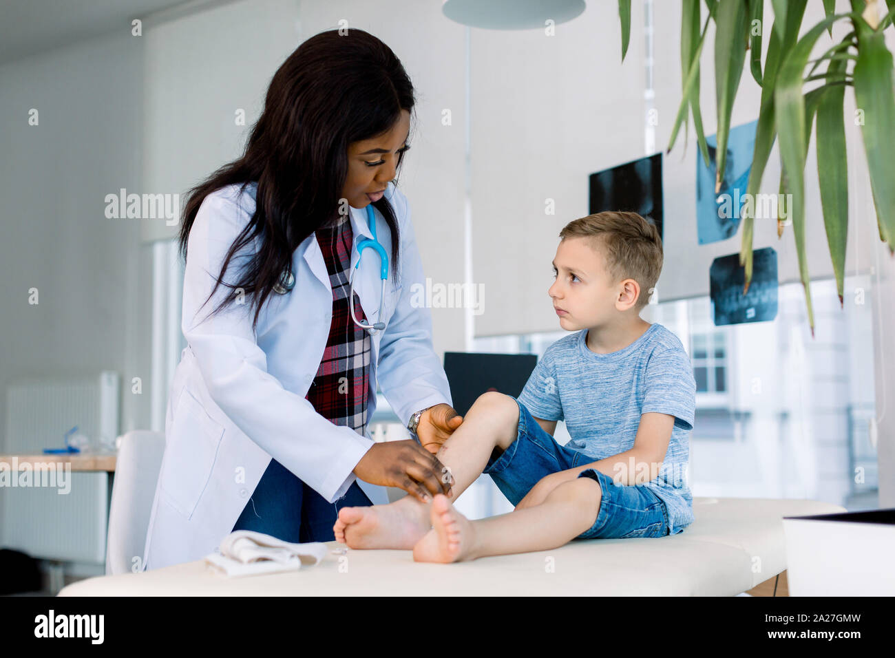 Female African American doctor examining little boy's injured leg in ...