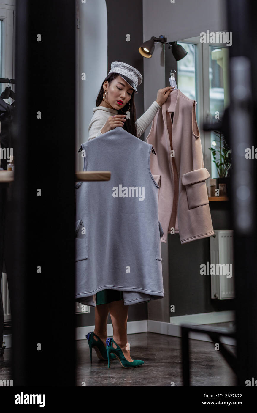 Concentrated young lady comparing two coats in the shop Stock Photo - Alamy
