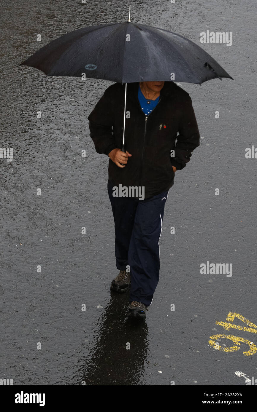 A man walks through heavy rain under an umbrella in Croydon, London ...