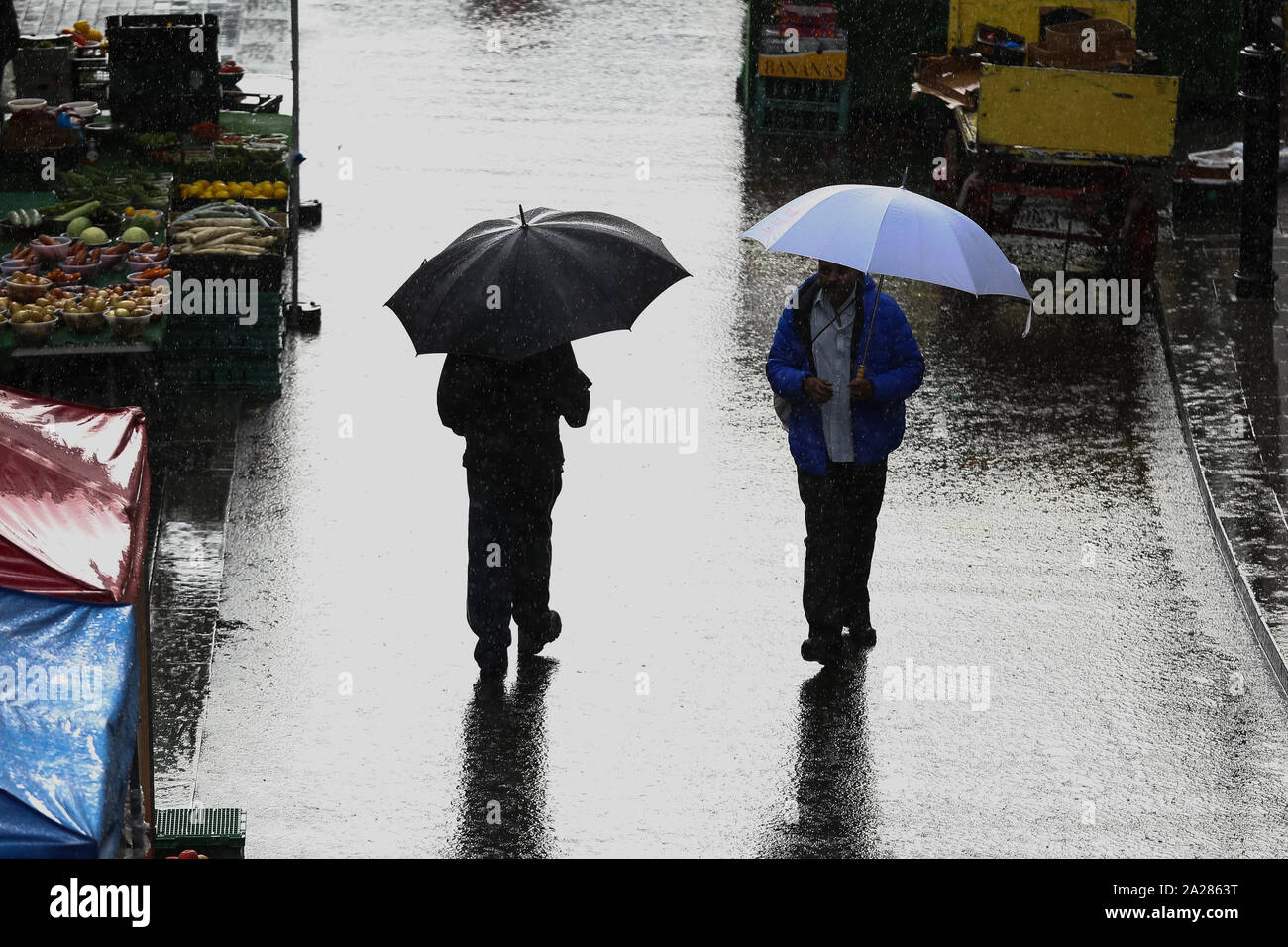 Two men walk through heavy rain under umbrellas in Croydon, London ...
