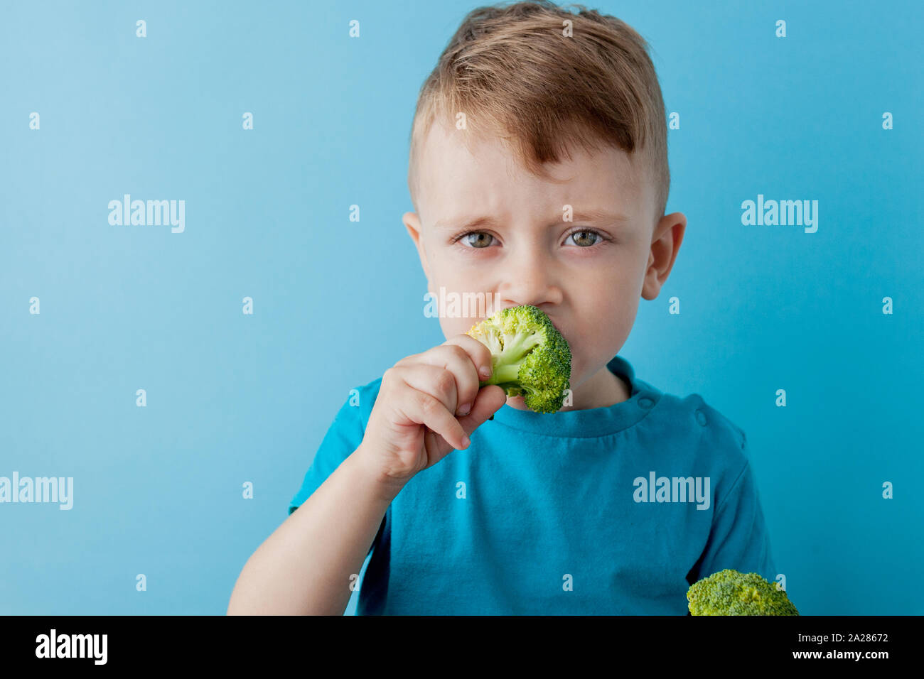 Little kid holding broccoli in his hands on blue background. Vegan and ...