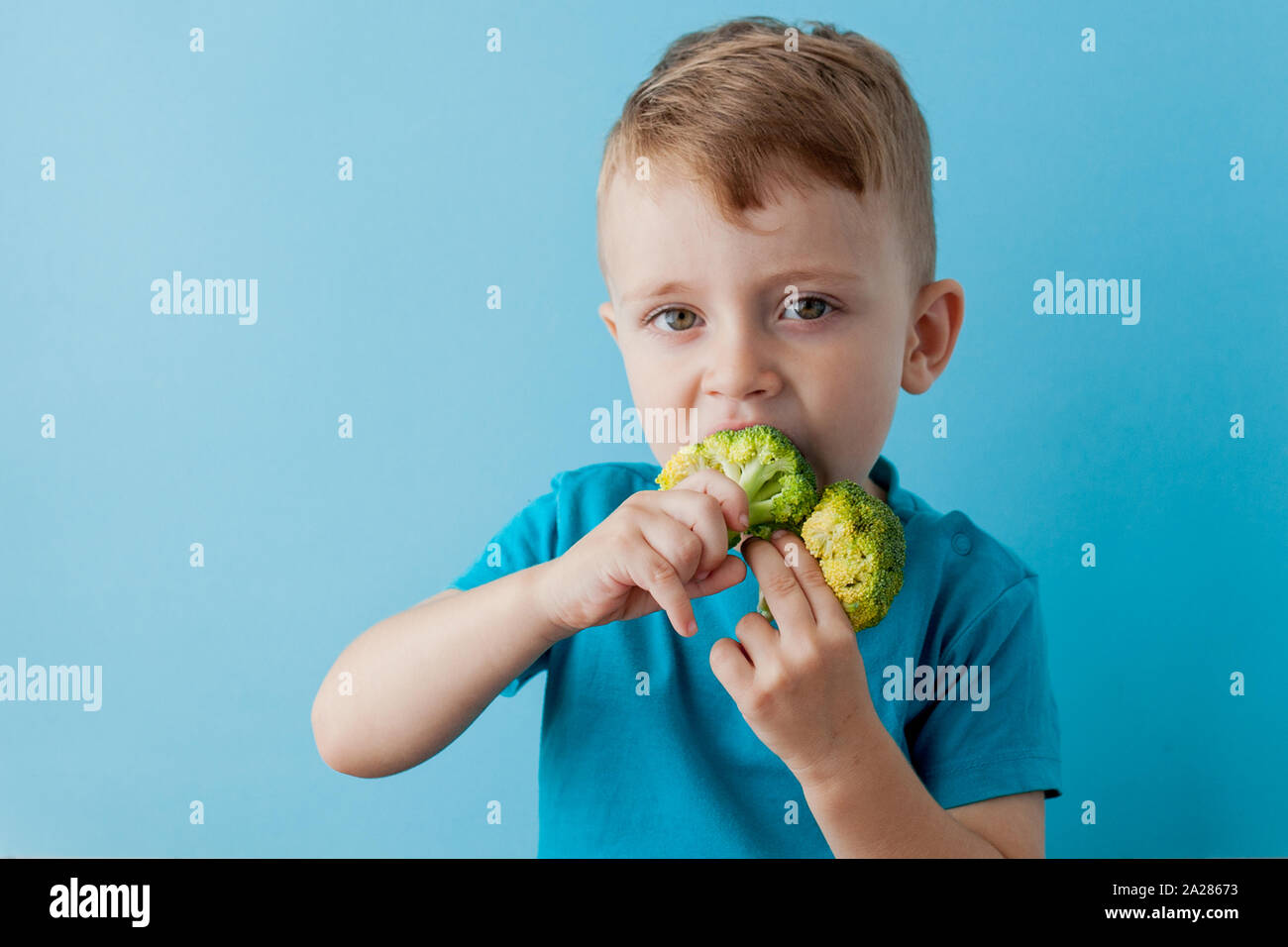 Little kid holding broccoli in his hands on blue background. Vegan and ...