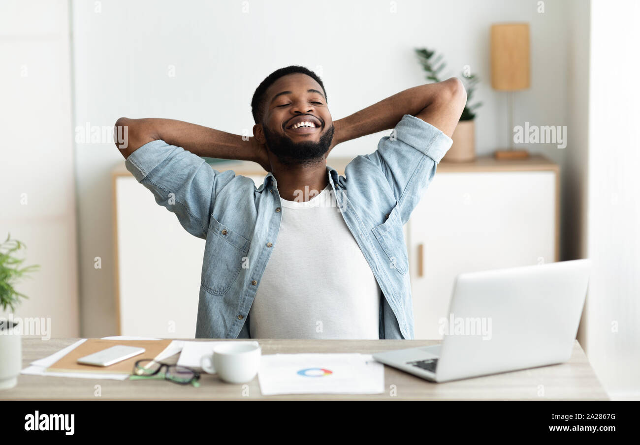 Cheerful employee sitting with hands behind head, relaxing in office ...