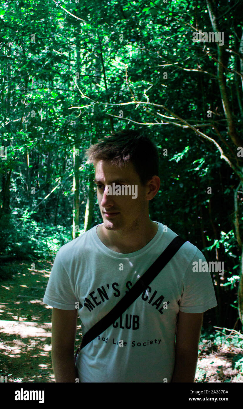 young boy surrounded by greenery with many shadows of tree branches ...