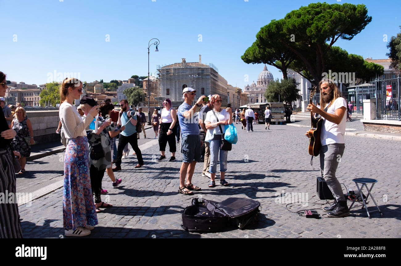 Young man busking with guitar and voice to an appreciative crowd of ...