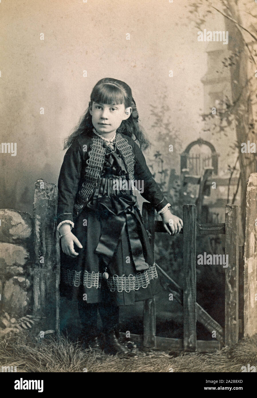 Archival image of a little girl standing outdoors by a gate wearing ...