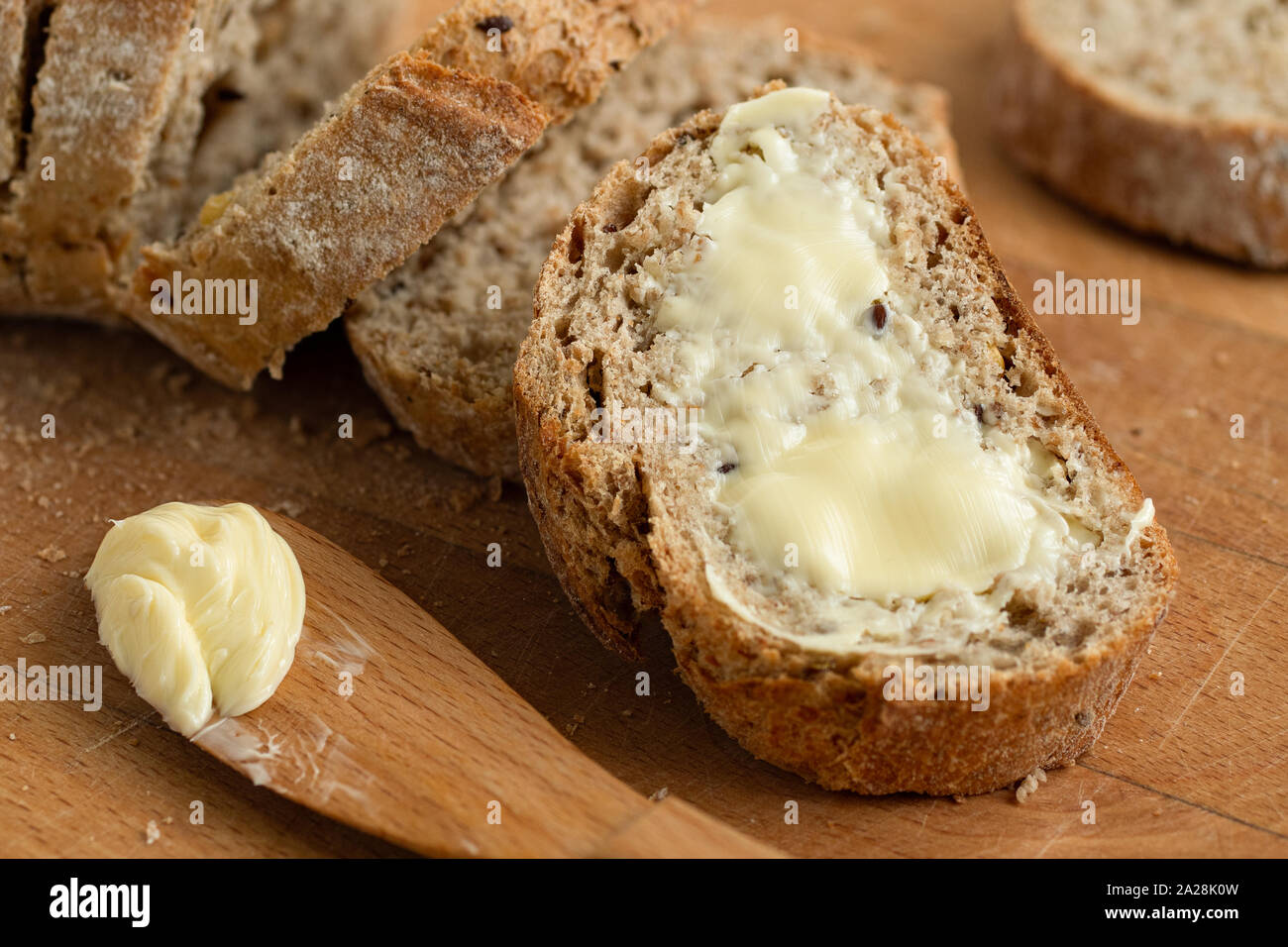 Closeup of buttered slice of whole wheat rustic bread next to cut bread ...