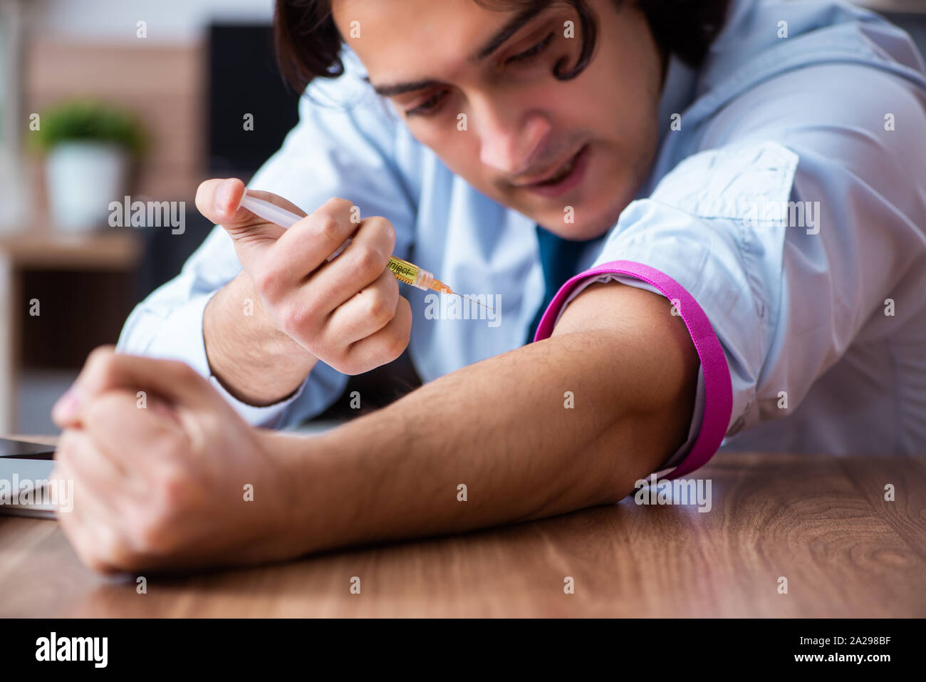 The young man having problems with narcotics at workplace Stock Photo ...