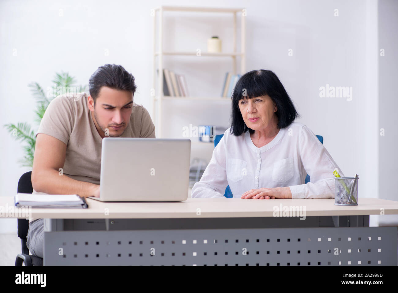 Young male employee explaining to old female colleague how to use ...