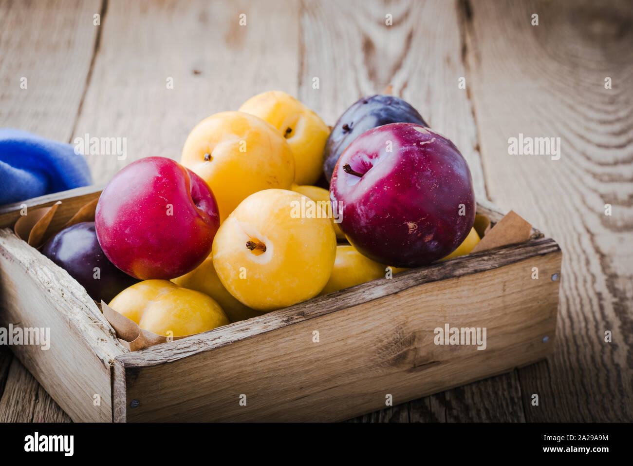 Colorful plums, fresh summer fruits in rural box. Plant based food ...