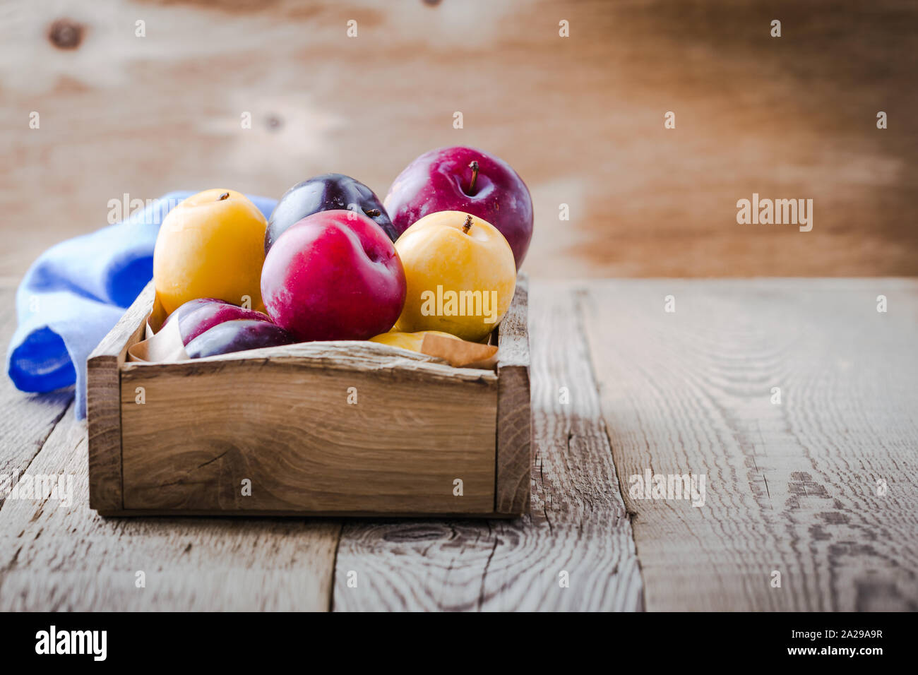 Colorful plums, fresh summer fruits in rural box. Plant based food ...