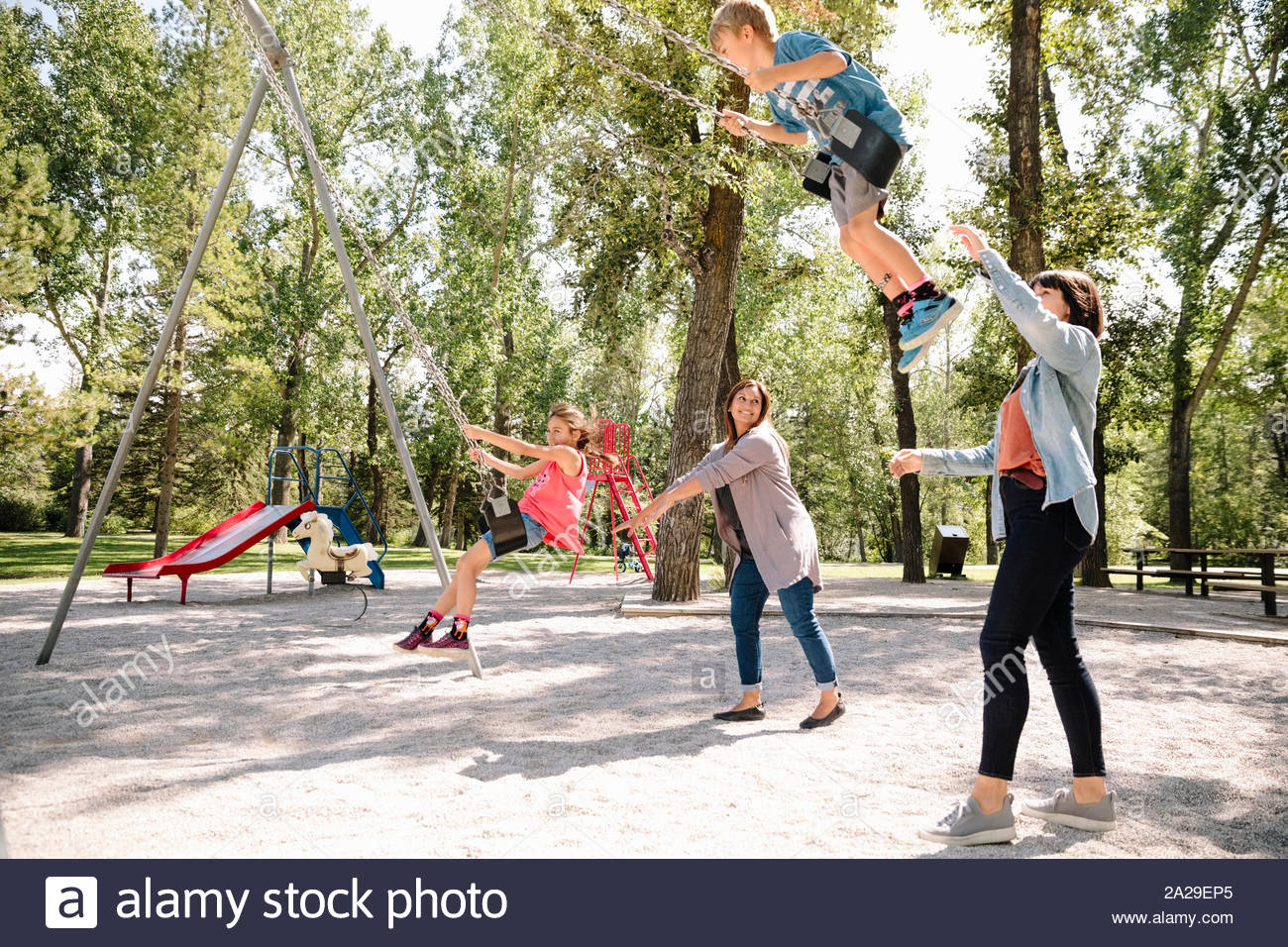 Children being pushed by mothers on swings in park Stock Photo - Alamy