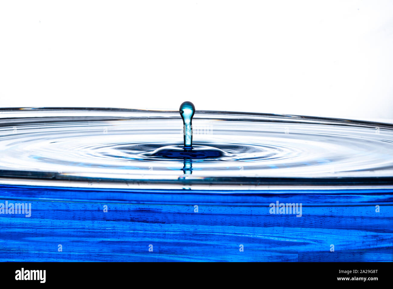 Single drop of water rises out of a calm pool surface into a leaning ...