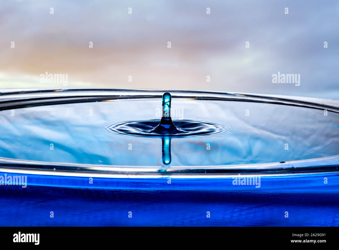 Single drop of water rises out of a calm pool surface into a rounded ...