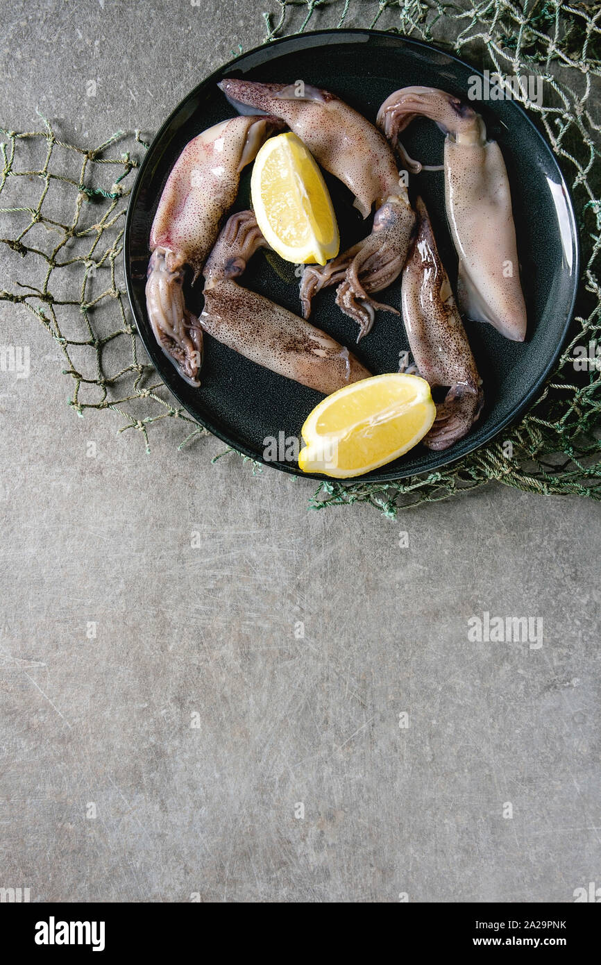 Raw uncooked squids calamari on ceramic plate with lemon and fishing ...