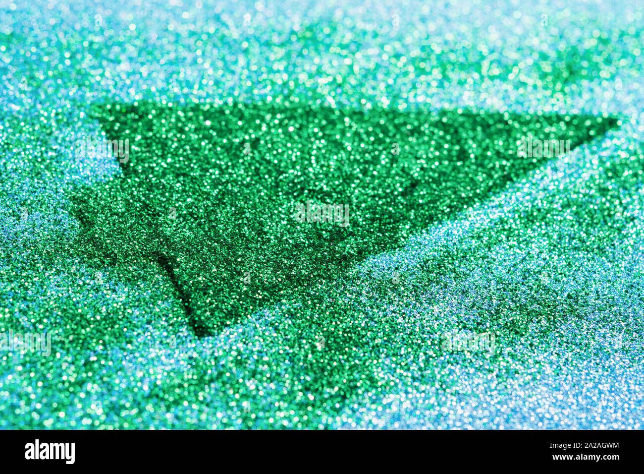 Green arrow shape made of glitter on sparkly blue paper, selective ...