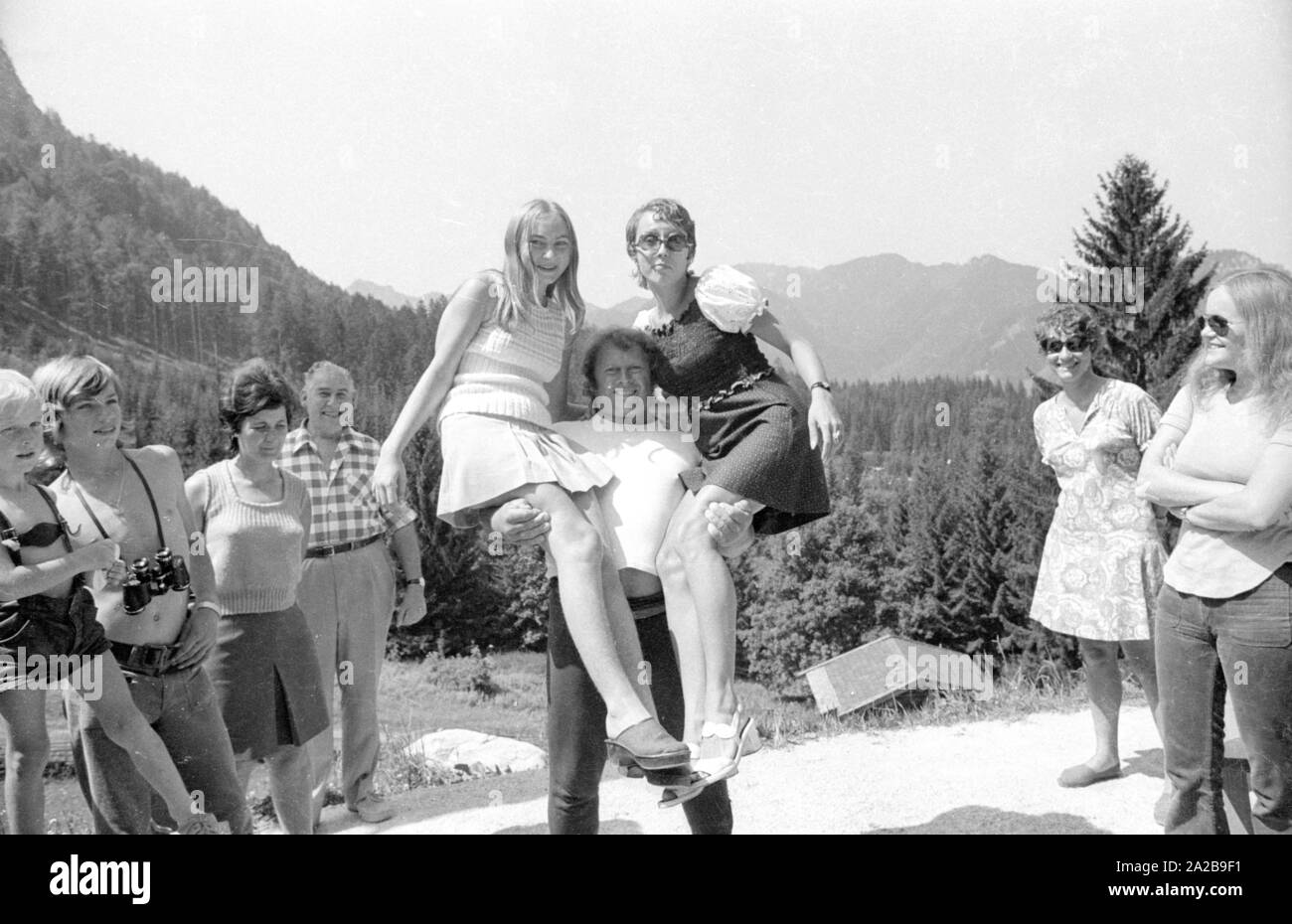 A stone lifter demonstrates his power by holding two women at the same ...