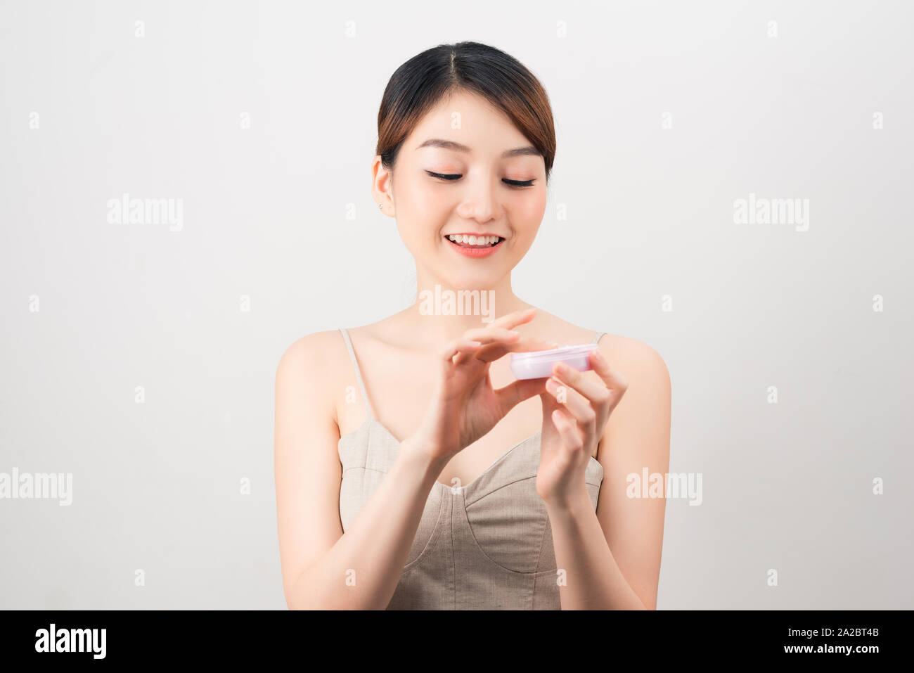 Cheerful young woman applying face cream isolated on white Stock Photo ...