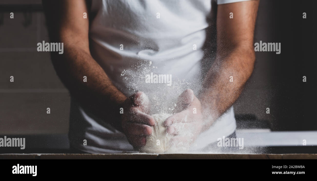 Man kneads raw dough, dust from flour flies in different directions ...