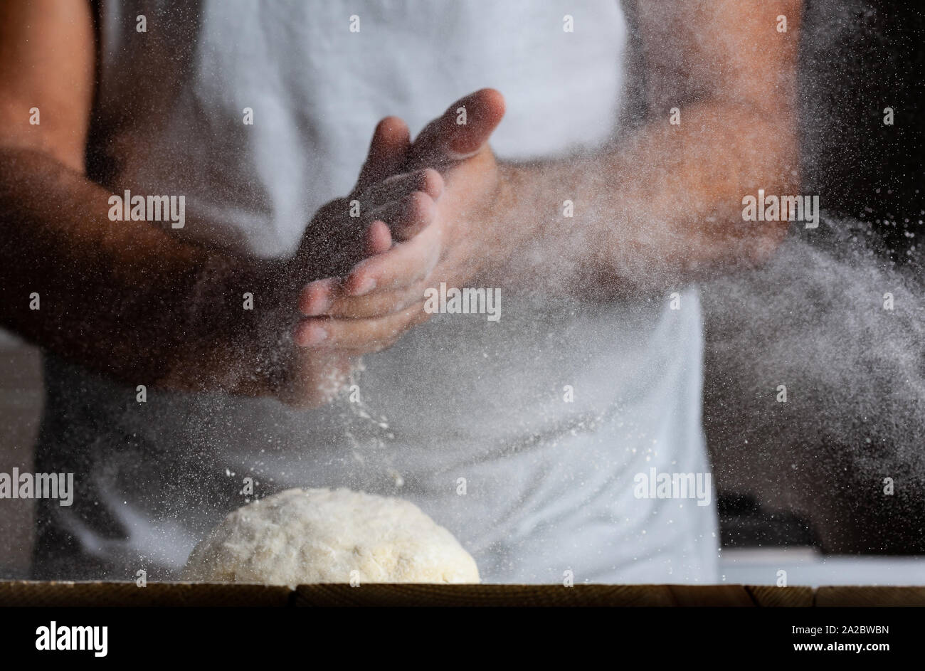 Man kneads raw dough, dust from flour flies in different directions ...