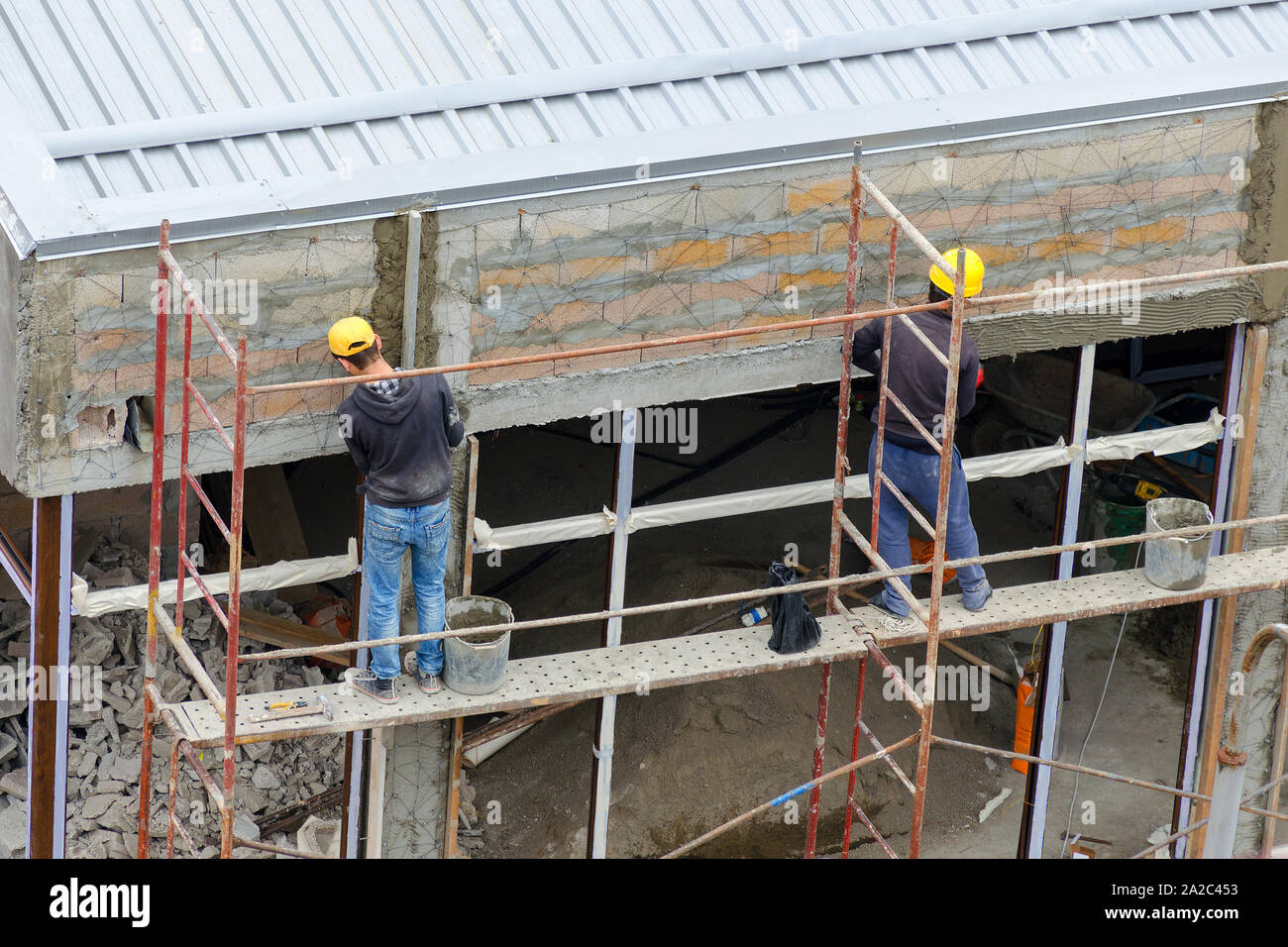 Two construction workers plaster a wall while standing on a scaffold ...