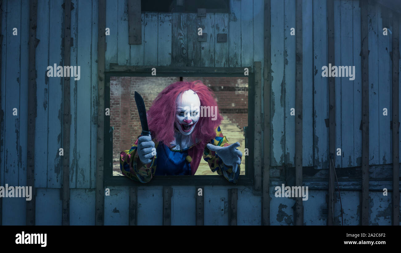 bad clown with a knife looks out of a window Stock Photo - Alamy