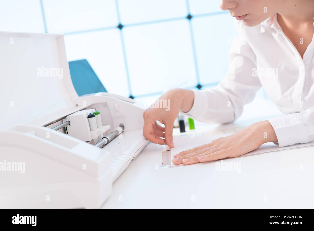 Young woman in printing office insert paper and color pens on plotter ...