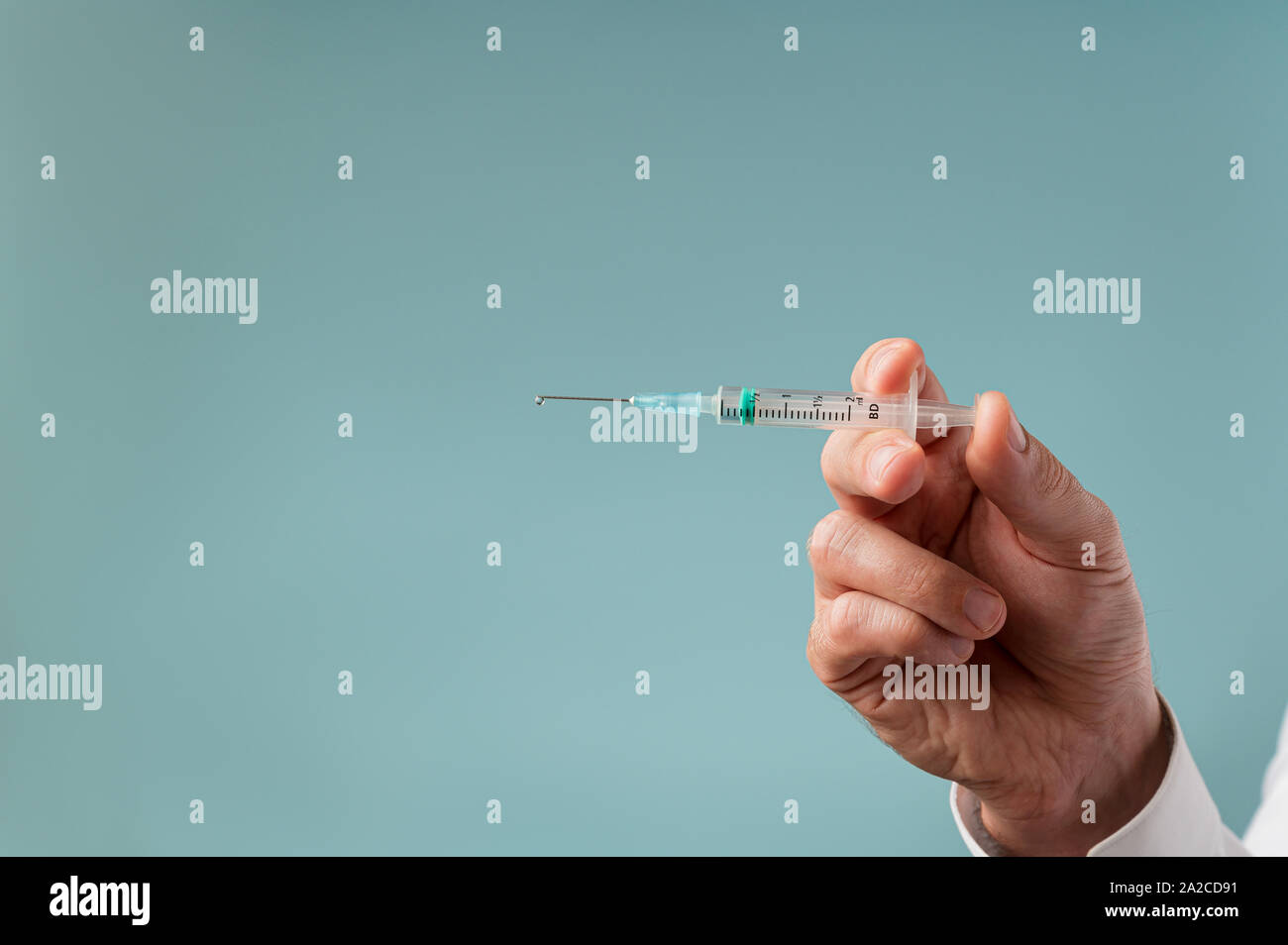 Male hand holding an injection with a drop at the end of a needle. Over ...