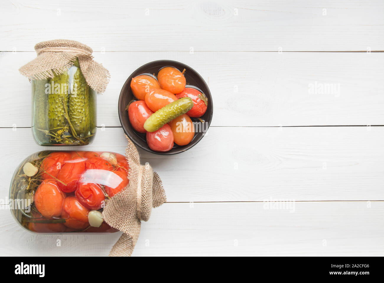 Canned vegetables cucumber and tomato in glass jars on white wooden ...