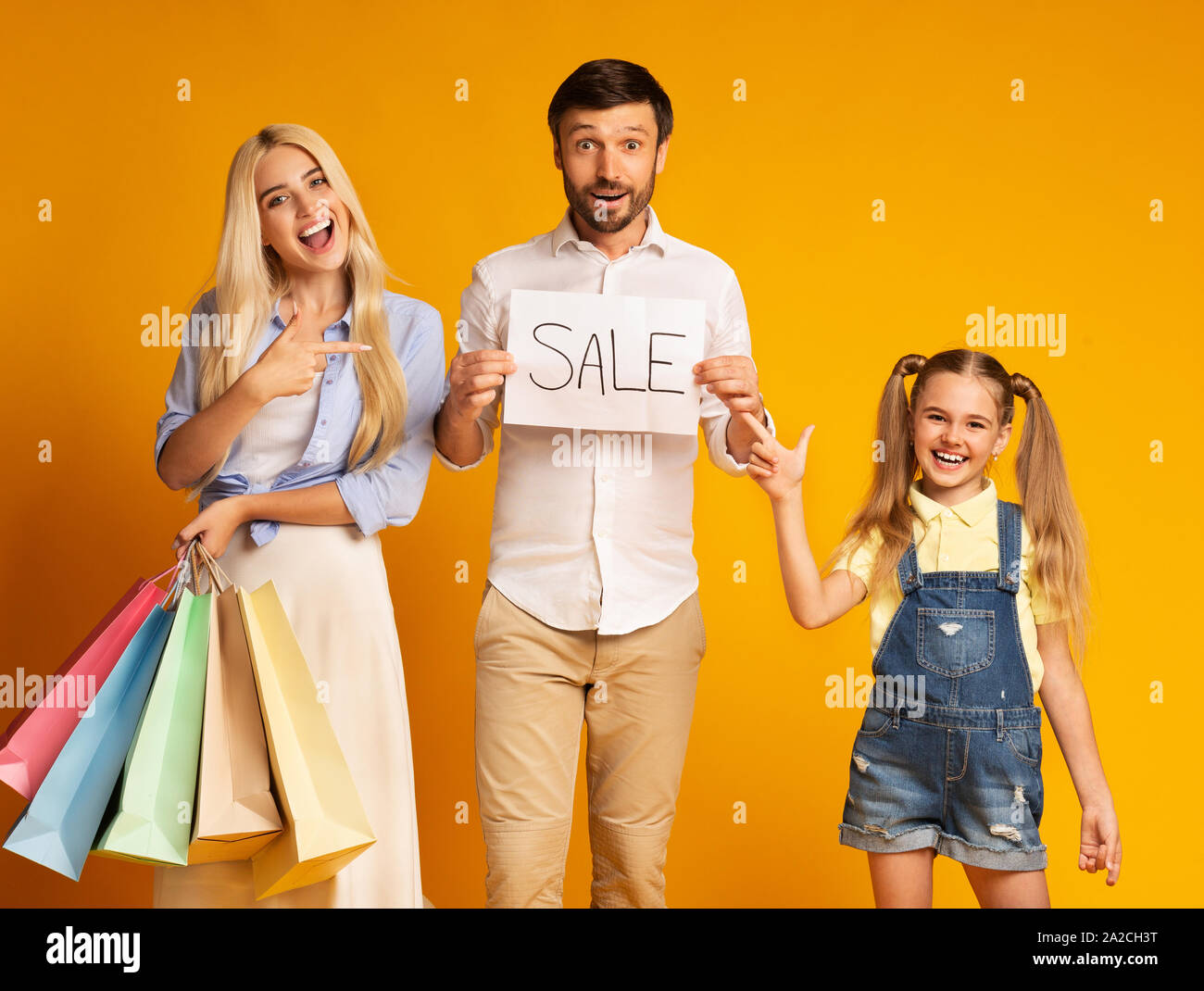 Family Showing Sale Sign Holding Shopping Bags Standing In Studio Stock ...
