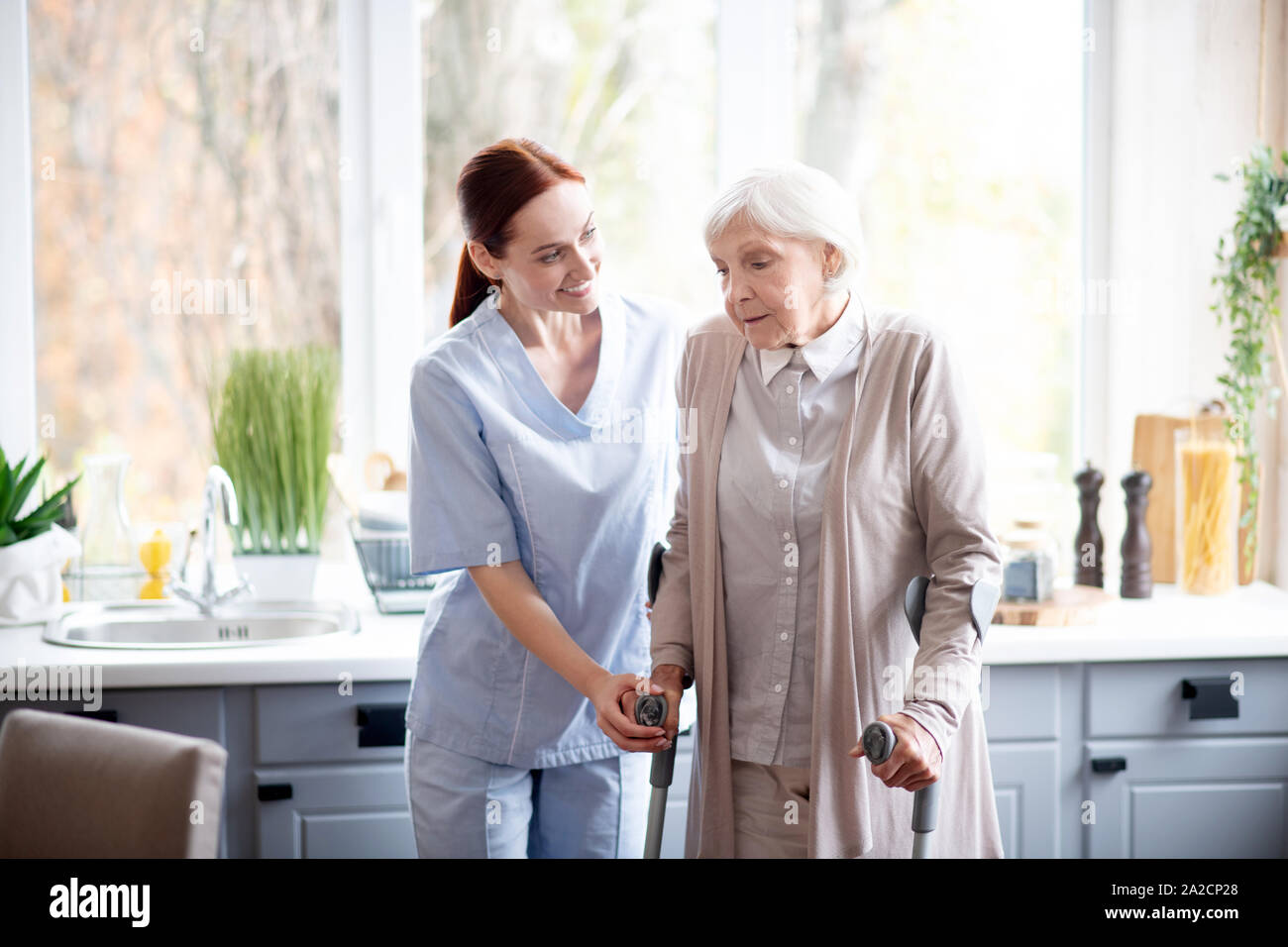 Smiling caregiver helping aged woman to make steps Stock Photo - Alamy