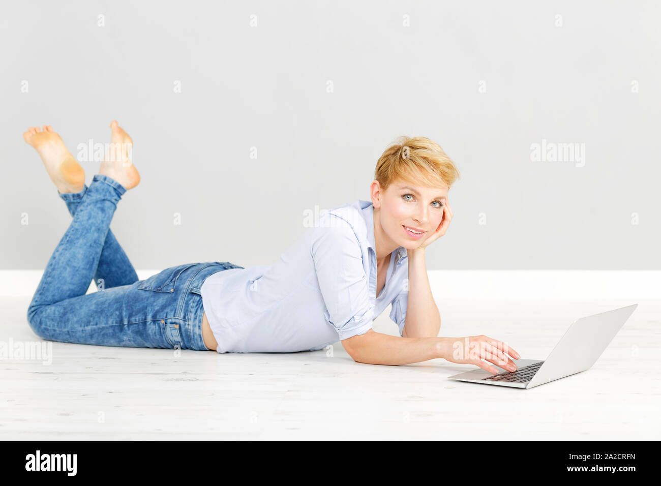 Attractive young woman using her laptop computer lying on the floor ...