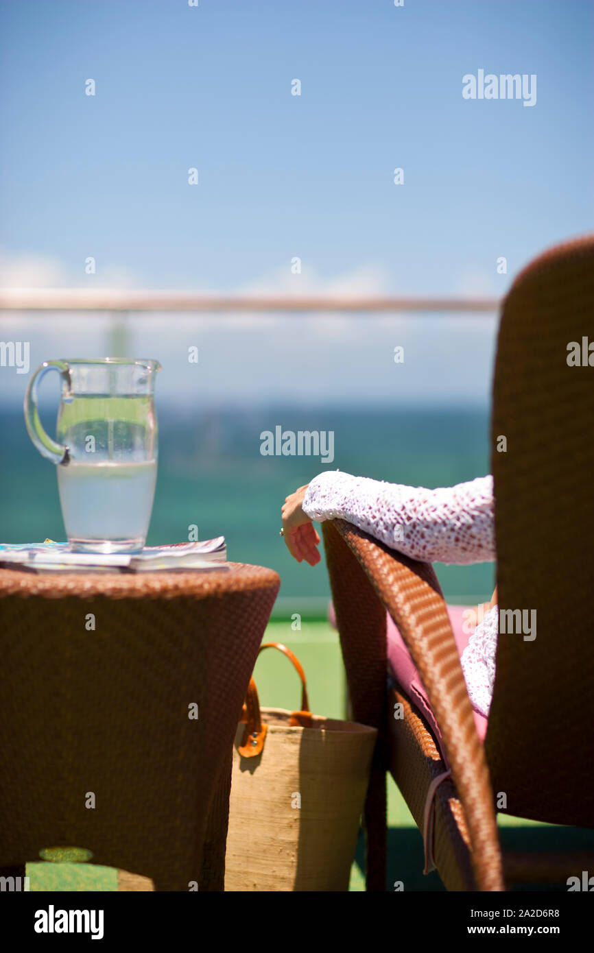 Woman relaxing in deck chair, with pitcher of ice water beside her ...
