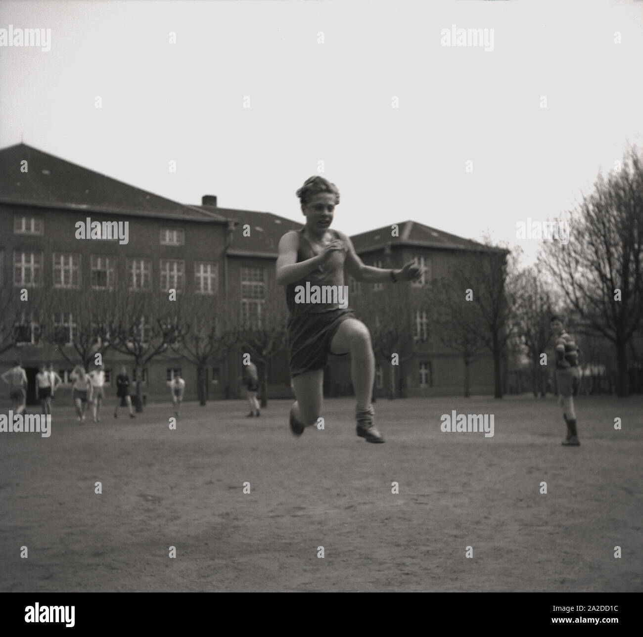 1960s, historical, a teenage boy in his sports kit doing a jump outside ...