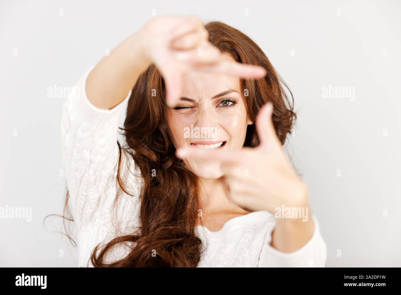 Beautiful young woman holding her hands up like a frame around her eyes ...