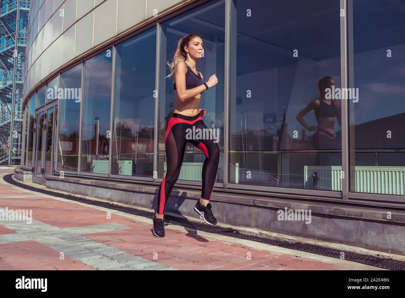 Beautiful girl athlete running jump in training, background glass ...