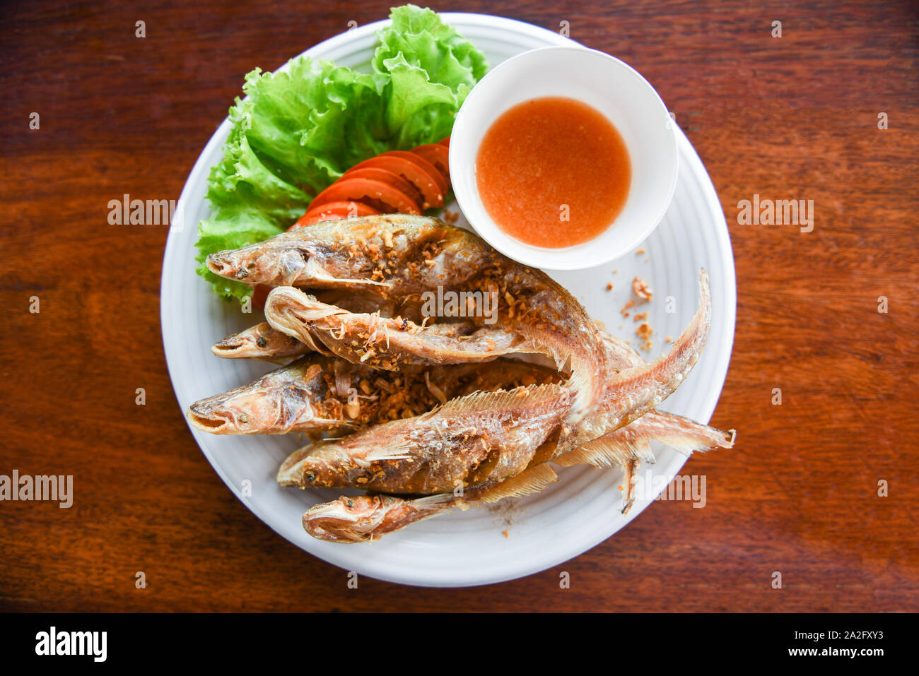 fried fish with vegetable salad tomato and sauce on white plate wooden ...