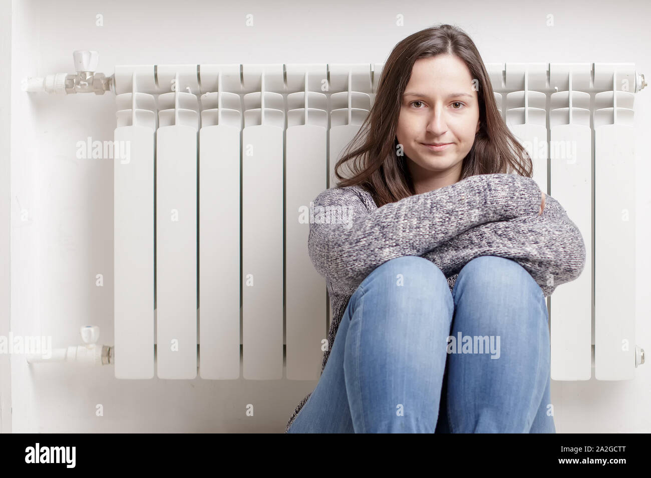 Young beautiful girl froze and warms hands near a radiator, dressed in ...