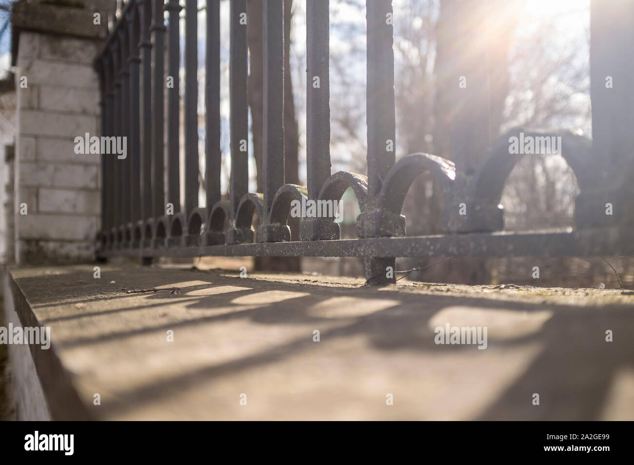 An ancient stone fence with a wrought-iron lattice in the rays of the ...