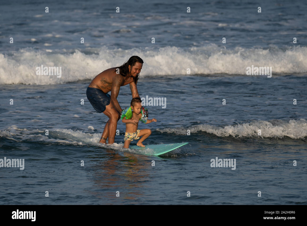 A father teaches his young son to surf at the famous Cloud 9 surf break ...